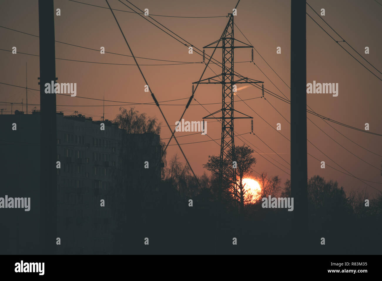 red sunset with sun setting down behind large electricity power line ...