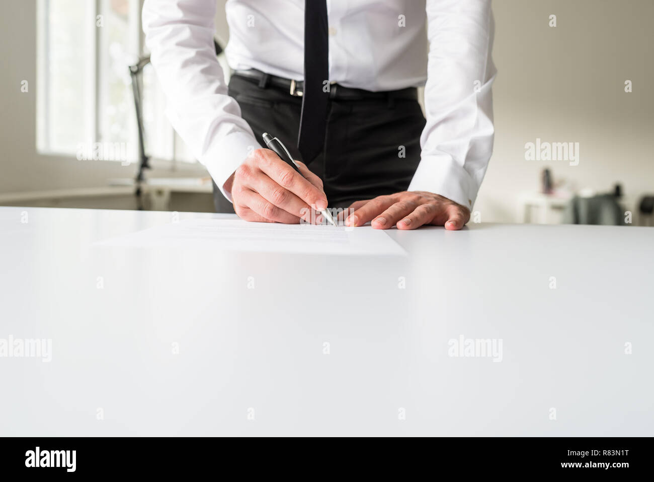 Front view of businessman standing behind his office desk signing a ...