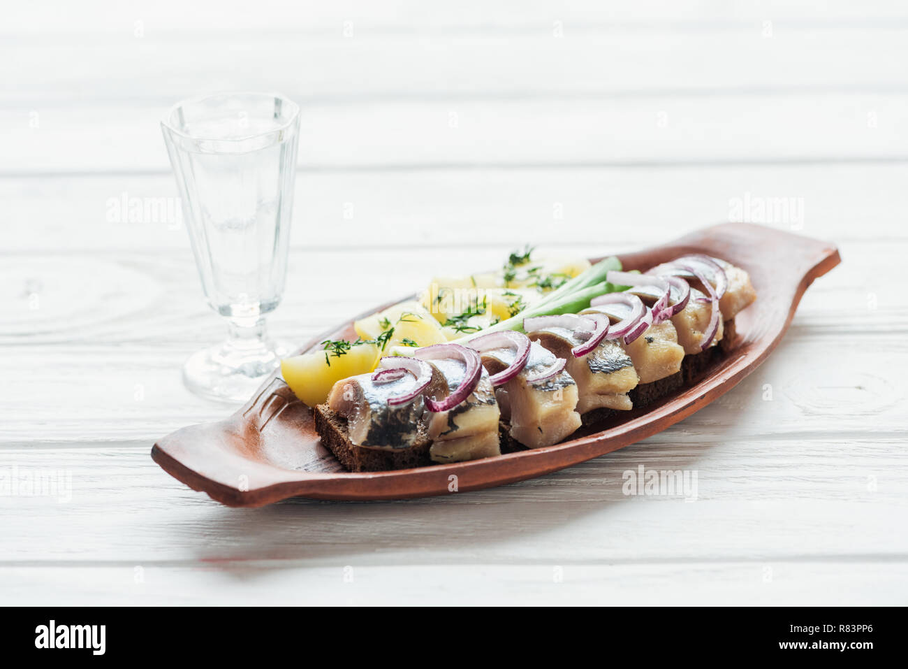 marinated herring, potatoes and onions in earthenware plate with glass ...