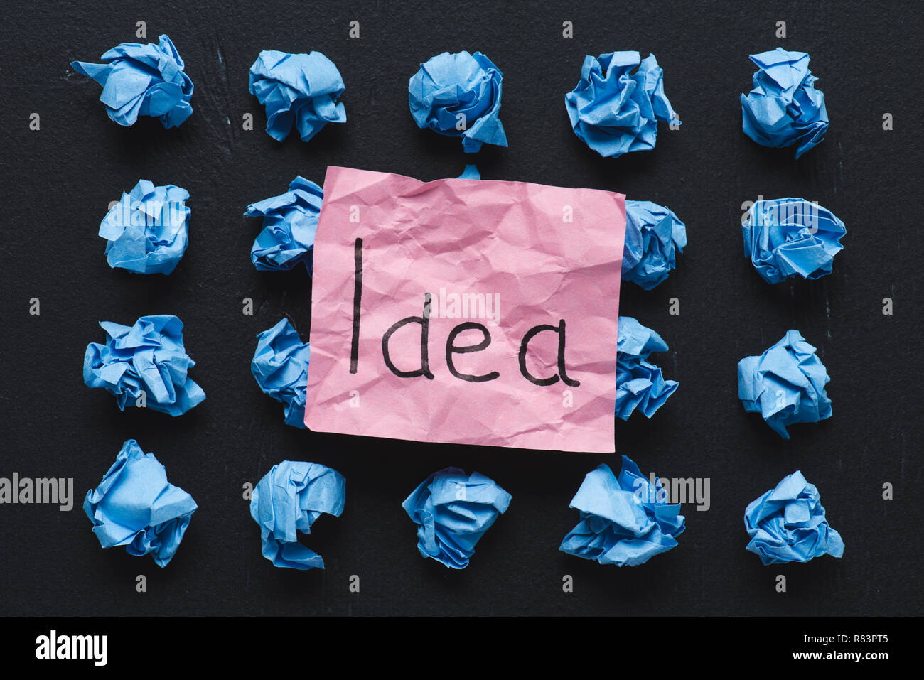 top view of 'idea' word written on sticky note with blue crumpled paper ...