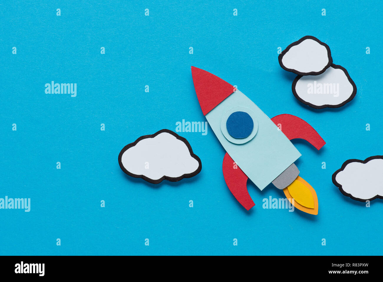 top view of cardboard rocket with clouds on blue background, setting ...