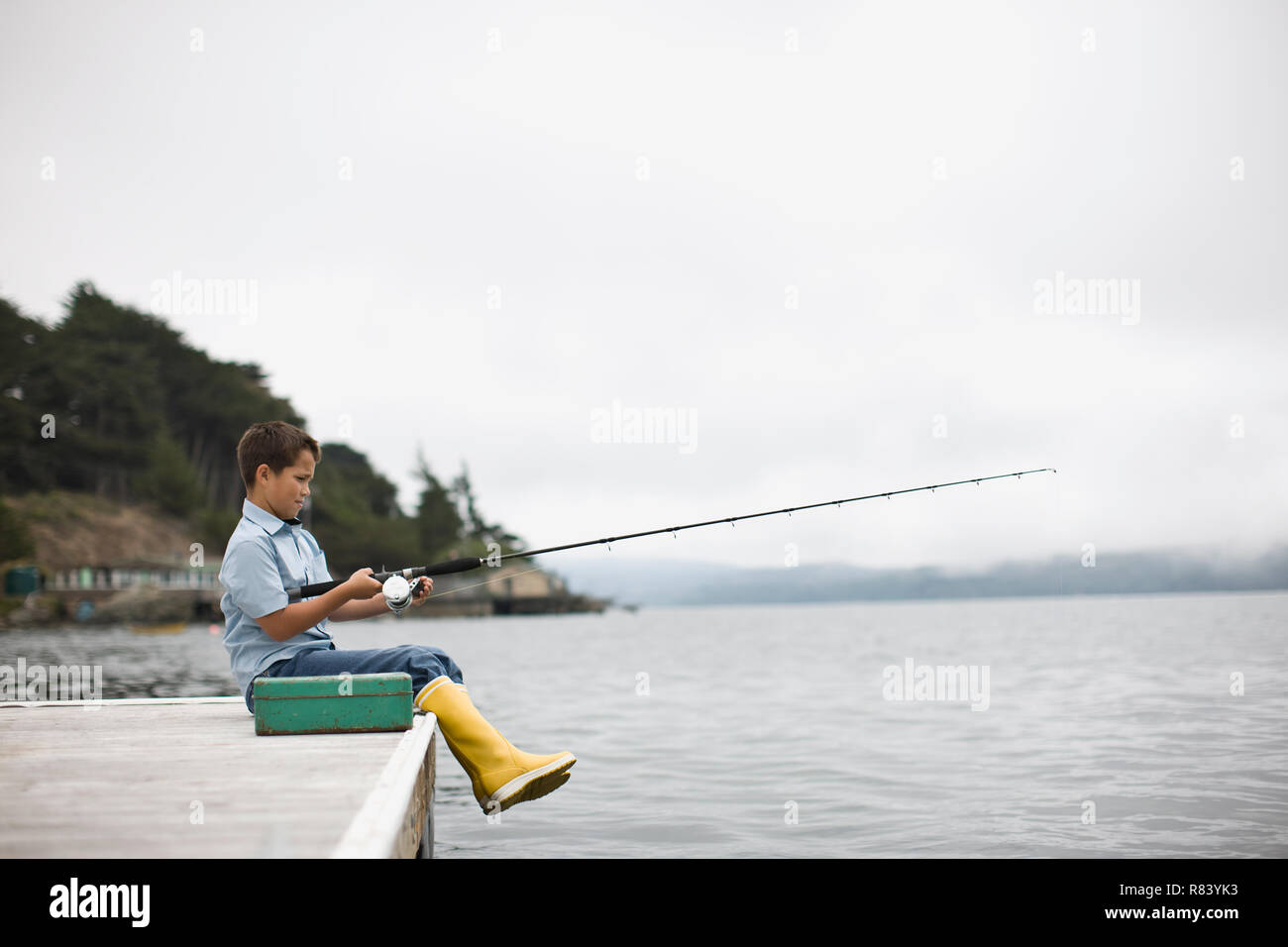 Boy fishing off the side of a jetty with a fishing rod Stock Photo - Alamy