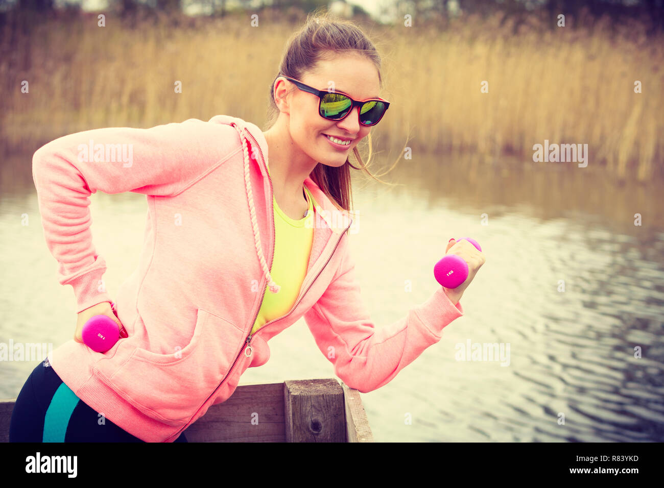 Woman doing sports outdoors with dumbbells lifting weights. Fit fitness ...