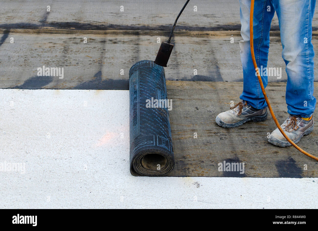 Roofer installing rolls of bituminous waterproofing membrane for the waterproofing of a terrace ...