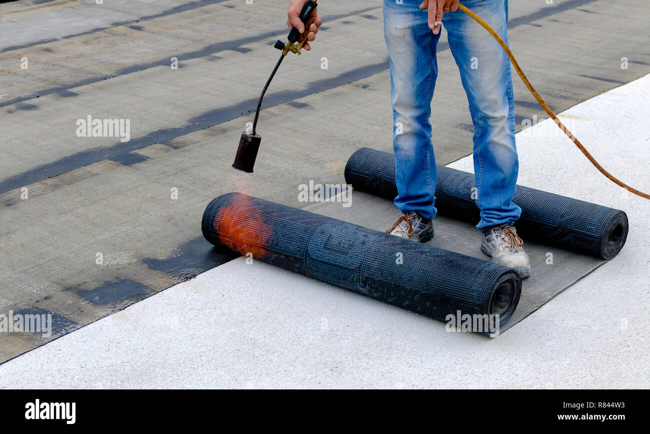 Roofer installing rolls of bituminous waterproofing membrane for the waterproofing of a terrace ...