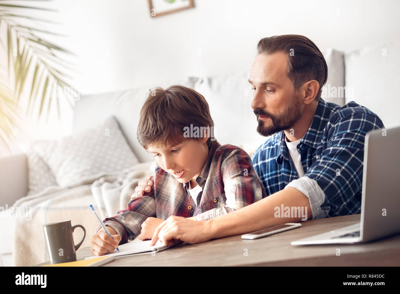 Father and son at home sitting at table dad showing boy how to do ...