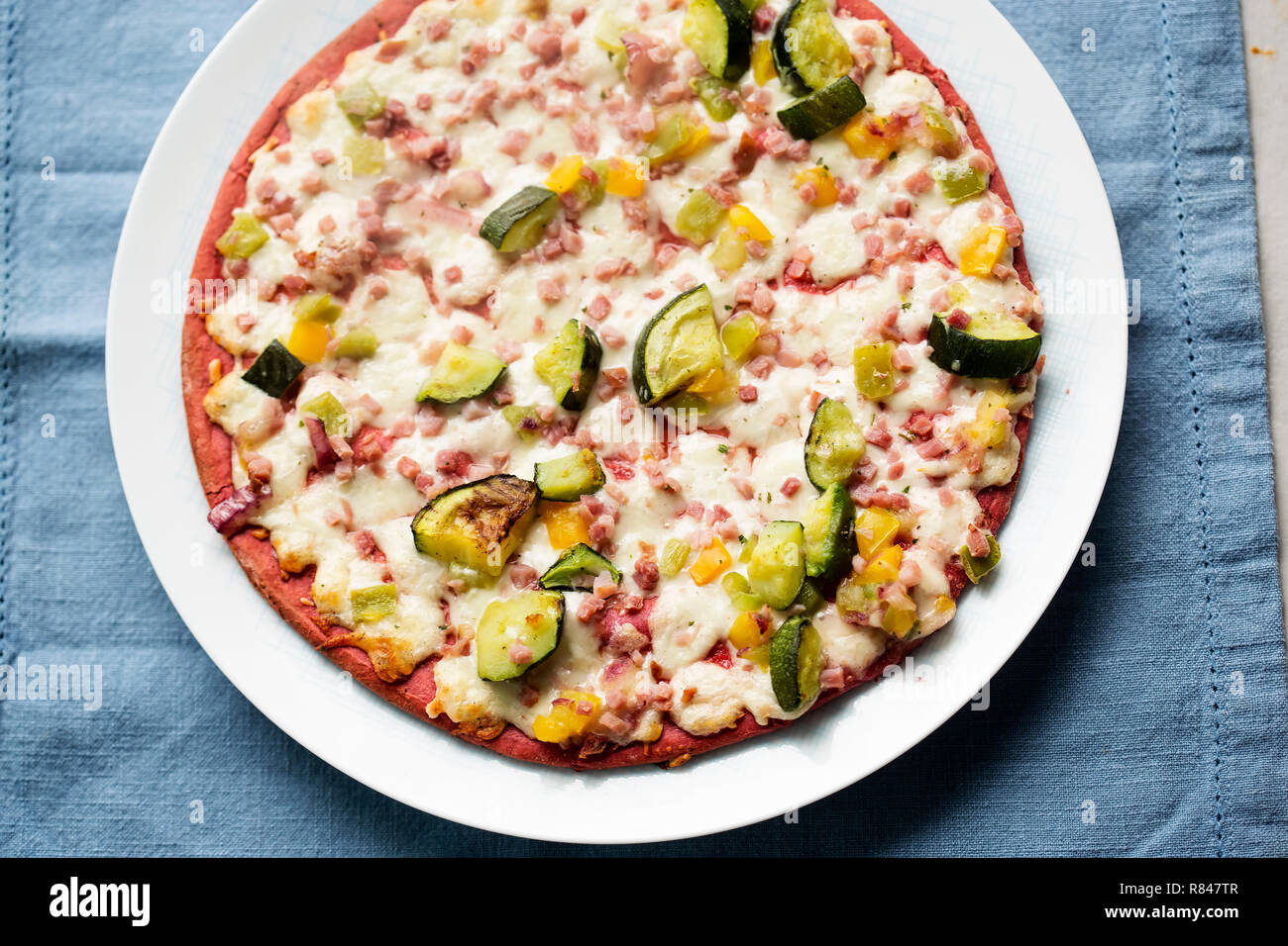Beetroot base pizza with zucchini, smoked ham, cheese & red onion Stock Photo - Alamy