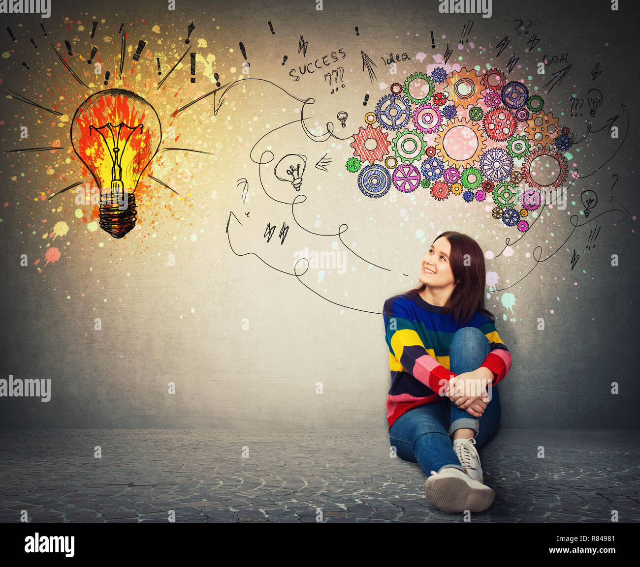 Young woman sitting on the floor smiling looking at a bright light bulb ...