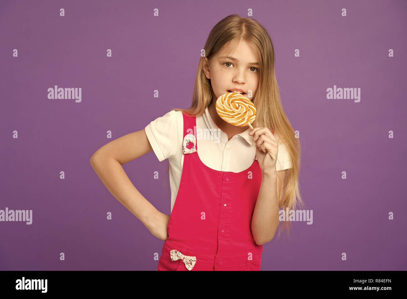 Kid eat lollipop on violet background. Little girl with swirl caramel ...