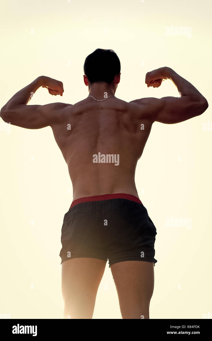 Man showing muscular body, back view. Bodybuilder posing on white sky ...