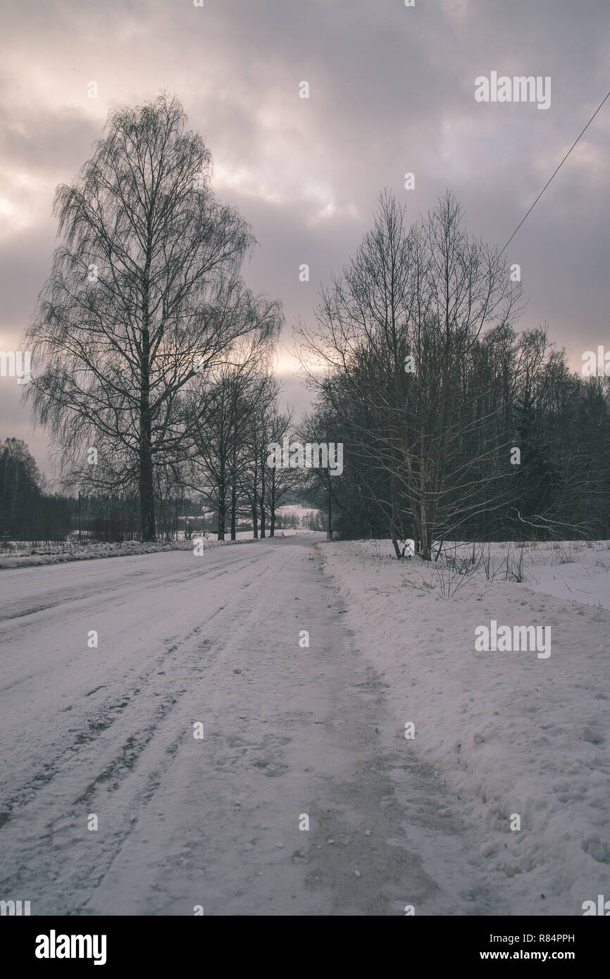 snow and ice covered road in countryside in winter with tire tracks ...