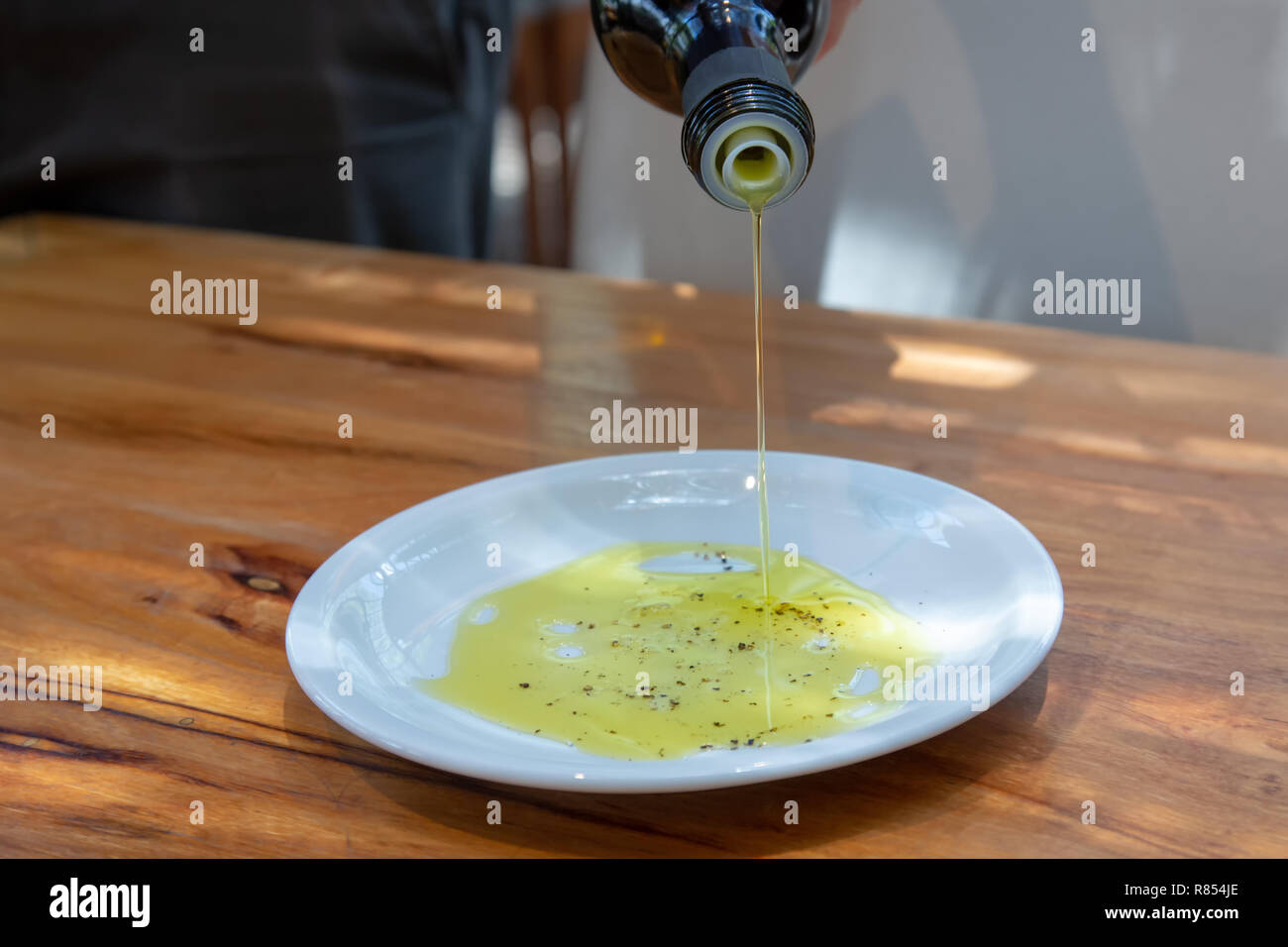 Pouring olive oil from a bottle to a white plate with fresh herbs on a ...
