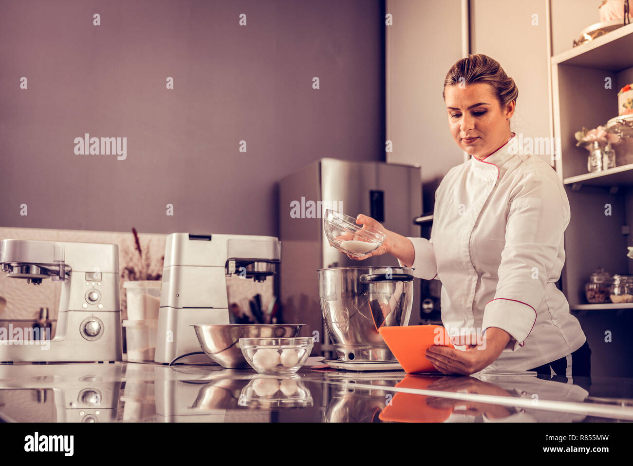 New recipe. Nice skilled chef looking at the tablet screen while trying ...