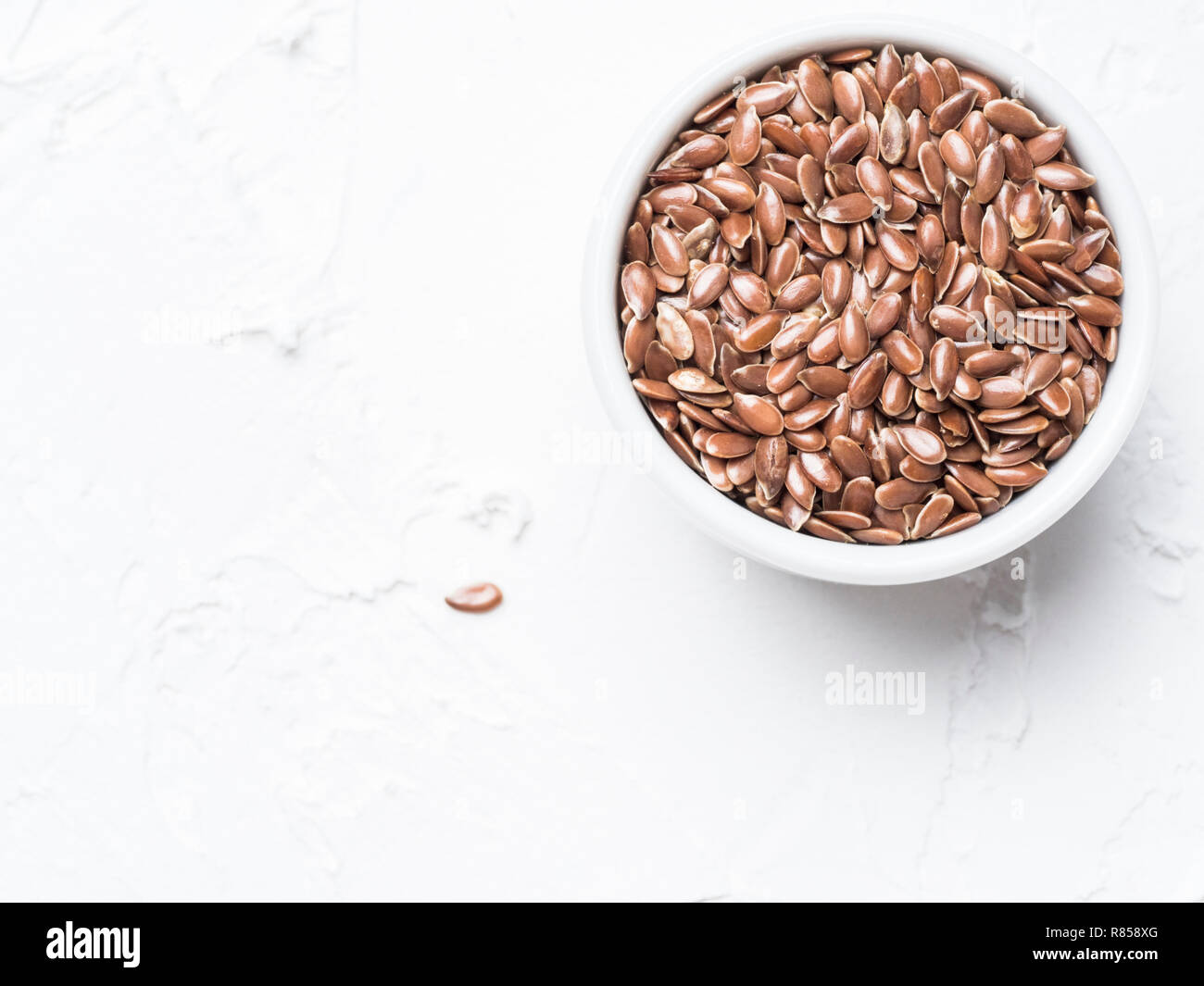 Flax seeds with copy space. Brown flax seed on white concrete textured background. Top view or ...