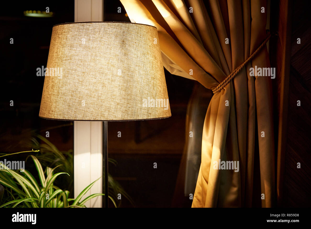 Classic lamp with dim light near window with gathered curtain at night ...
