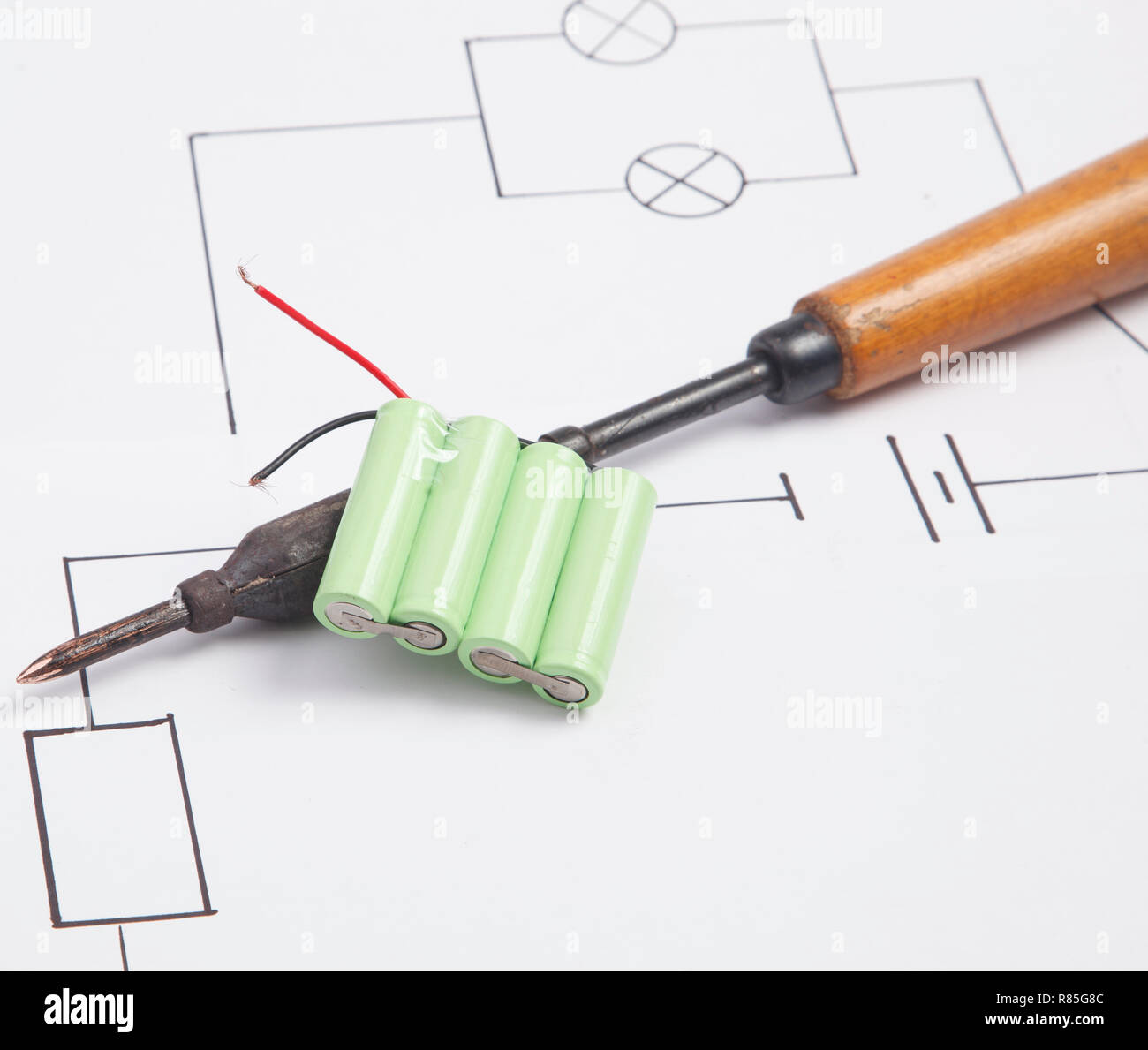 A soldering iron and battery on a background of the electric scheme ...