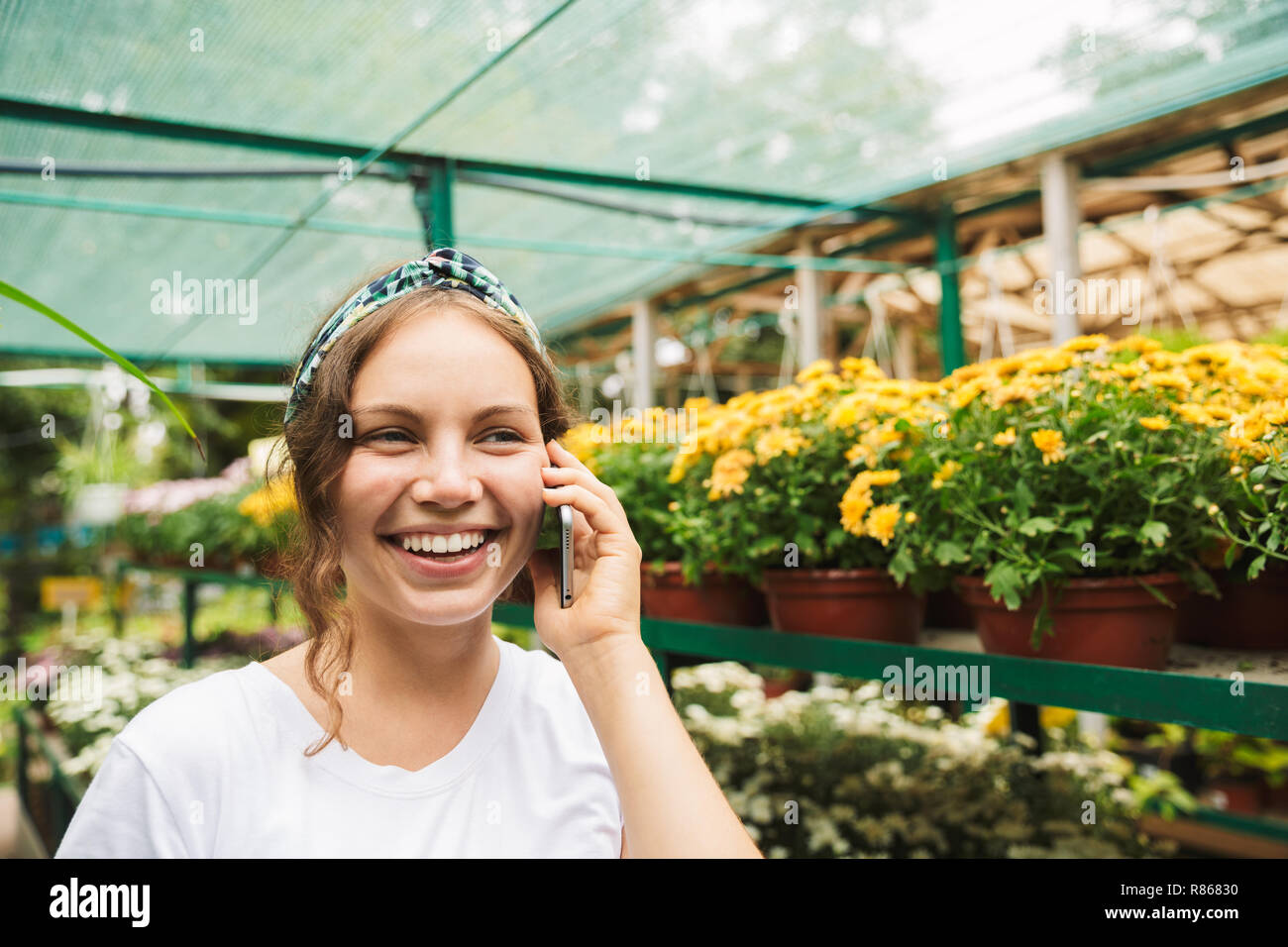 Cheerful young woman gardener talking on mobile phone while standing inside a greenhouse Stock ...