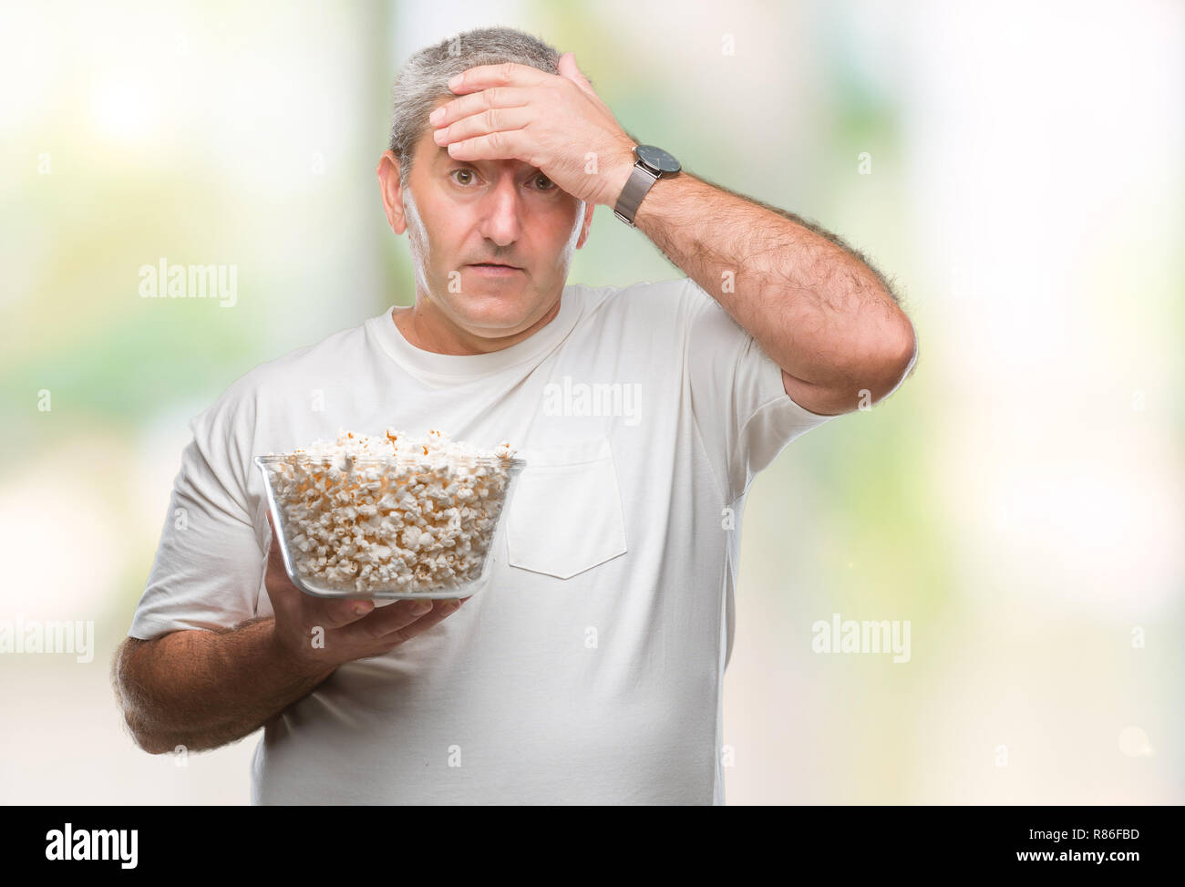 Handsome senior man eating popcorn over isolated background stressed ...