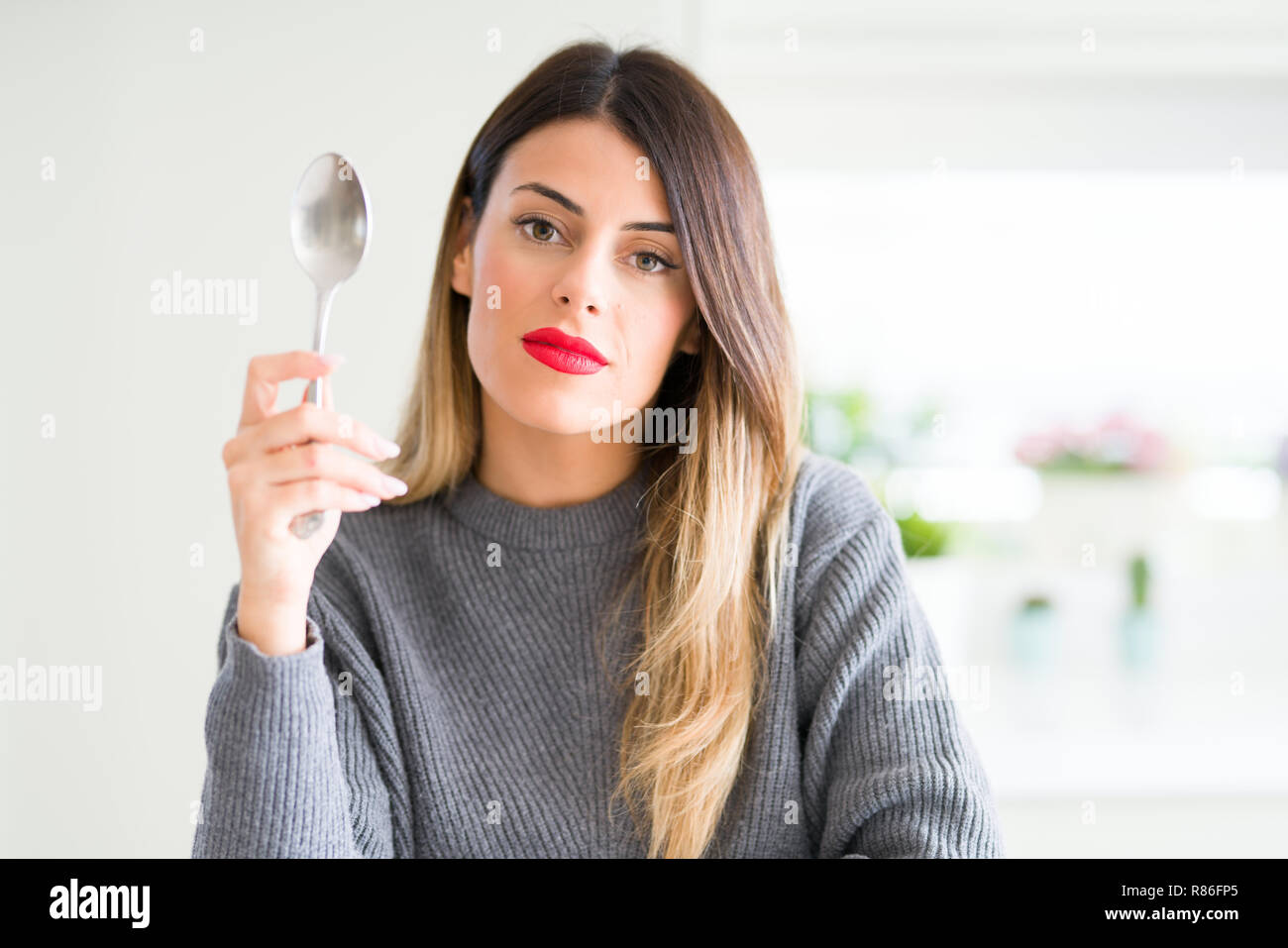 Young beautiful woman holding silver spoon at home with a confident ...