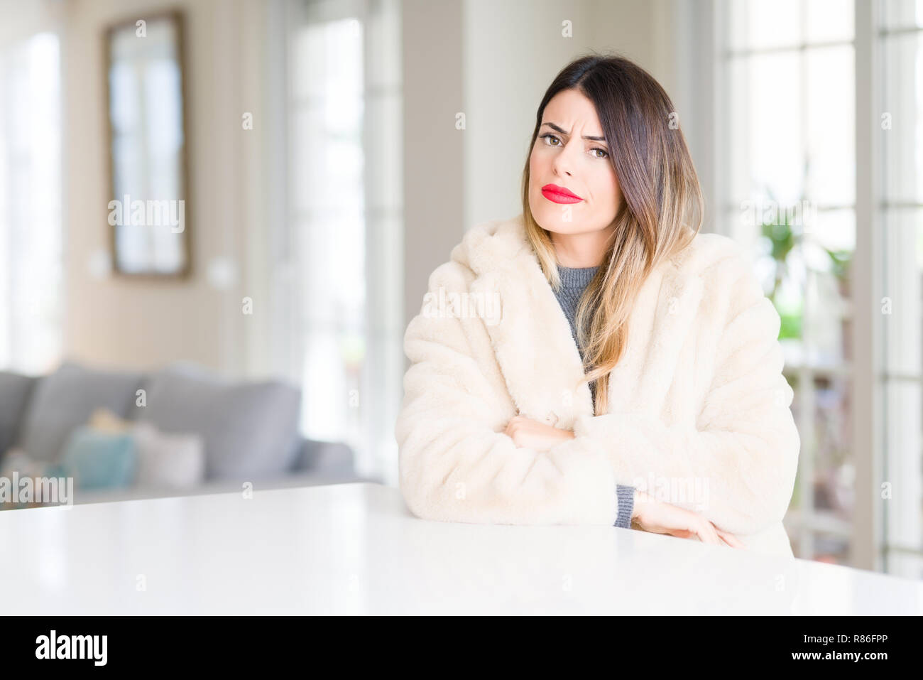 Young beautiful woman wearing winter fur coat at home skeptic and ...