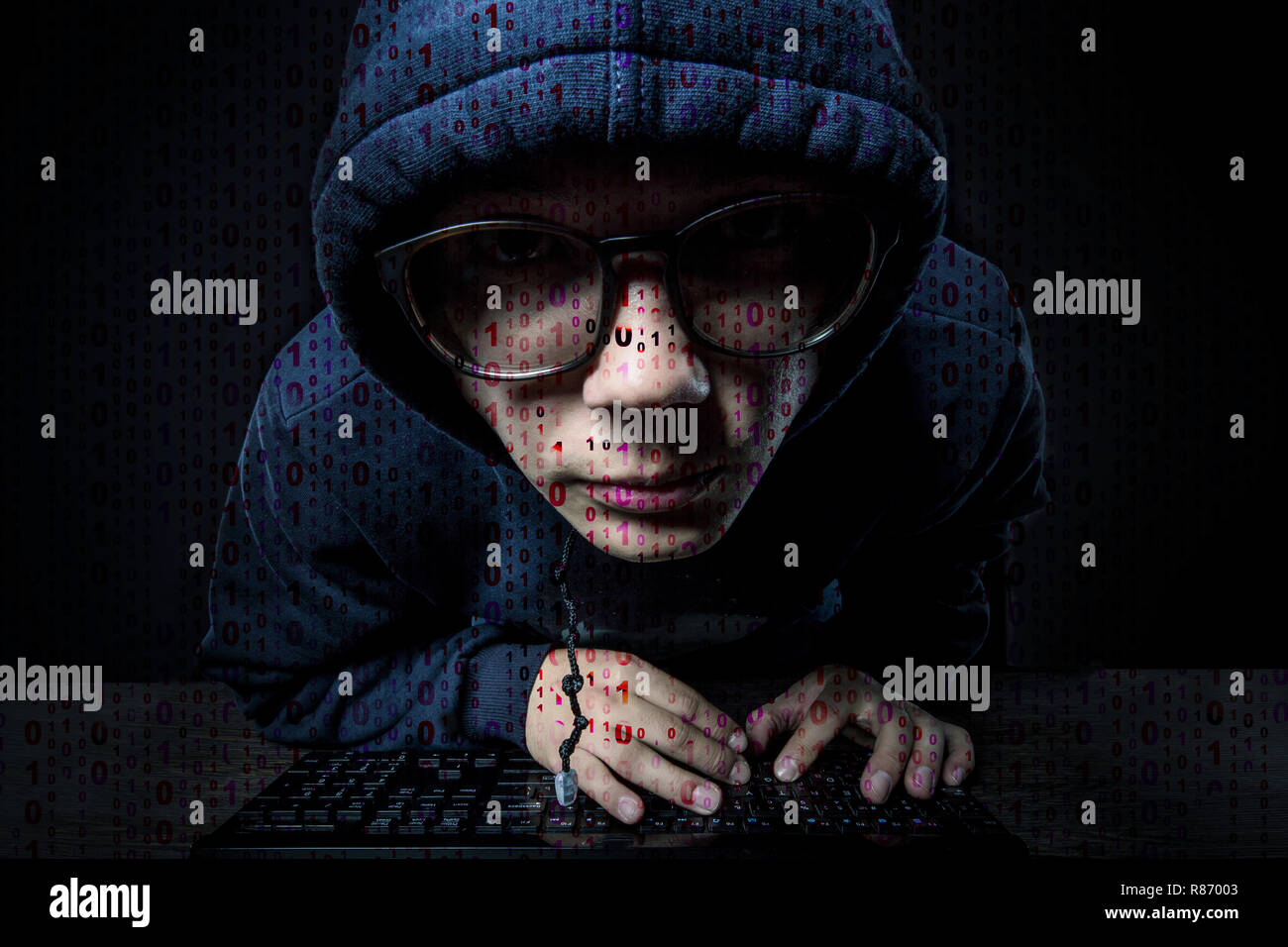binary code on the background of a hacker in a hood and glasses sits at ...