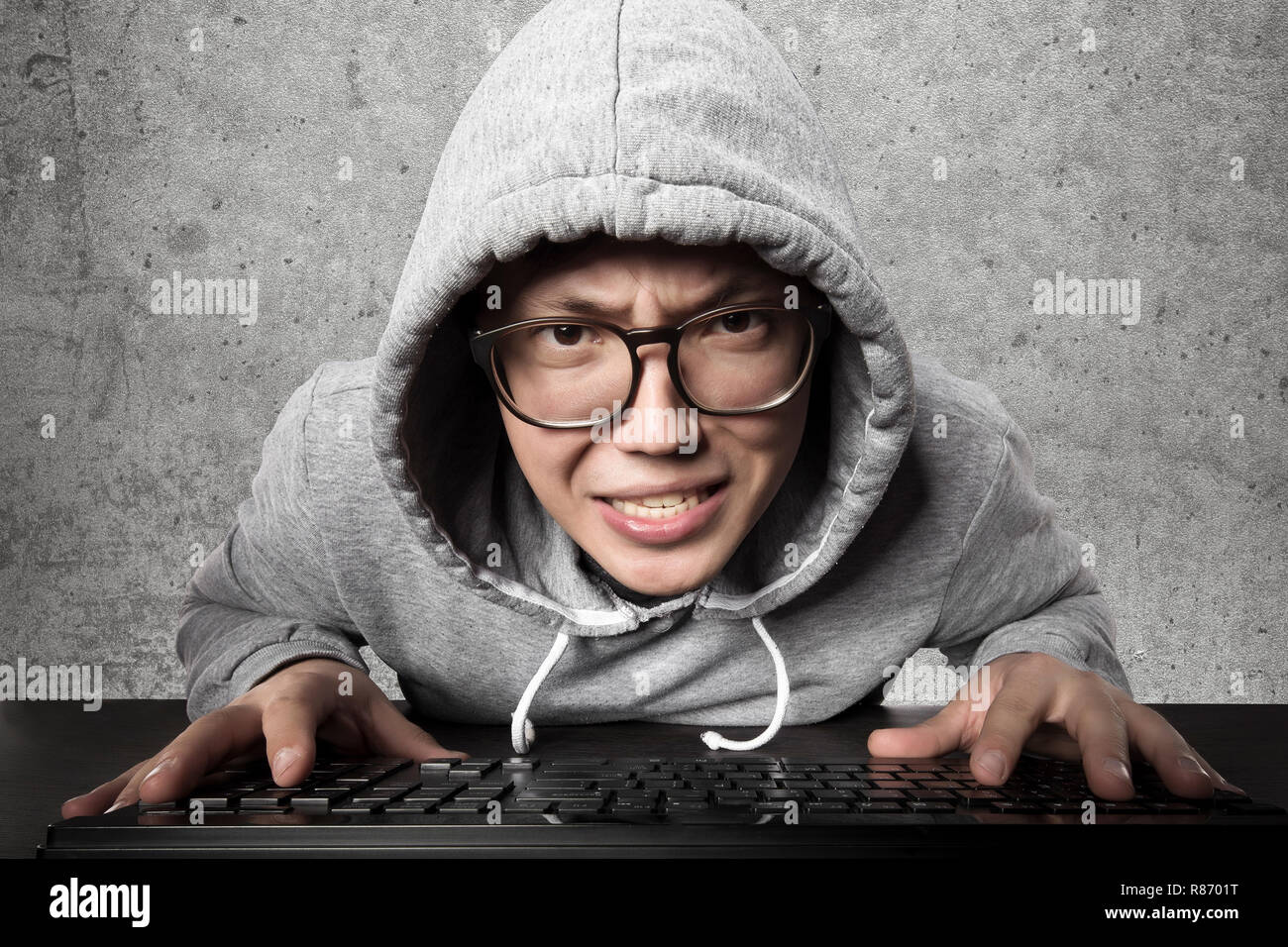 a perturbed programmer with glasses and a hood in front of the keyboard ...