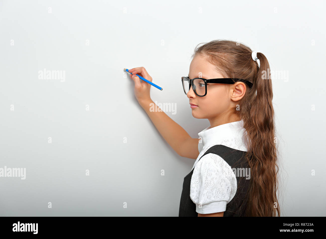 Smart pupil kid girl in eyeglasses looking on the blue wall background ...