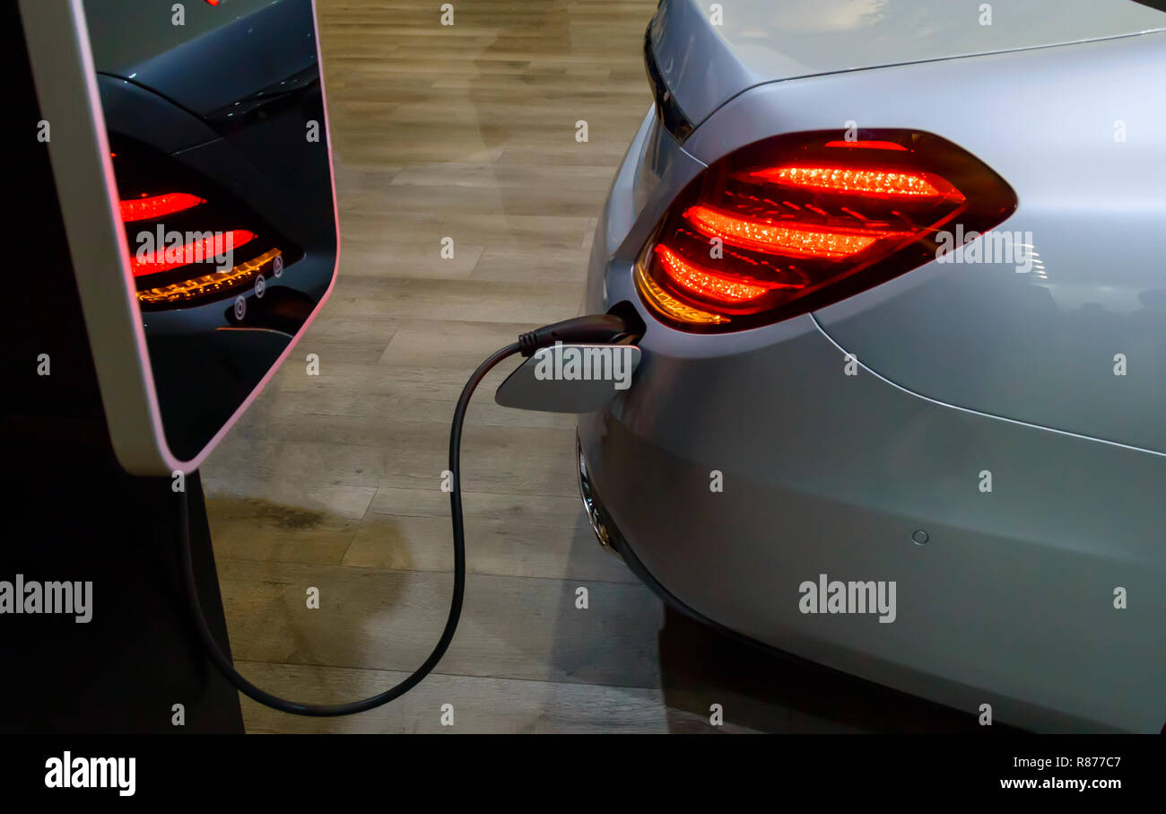 Silver electric car with a plugged in power cable at charging station ...