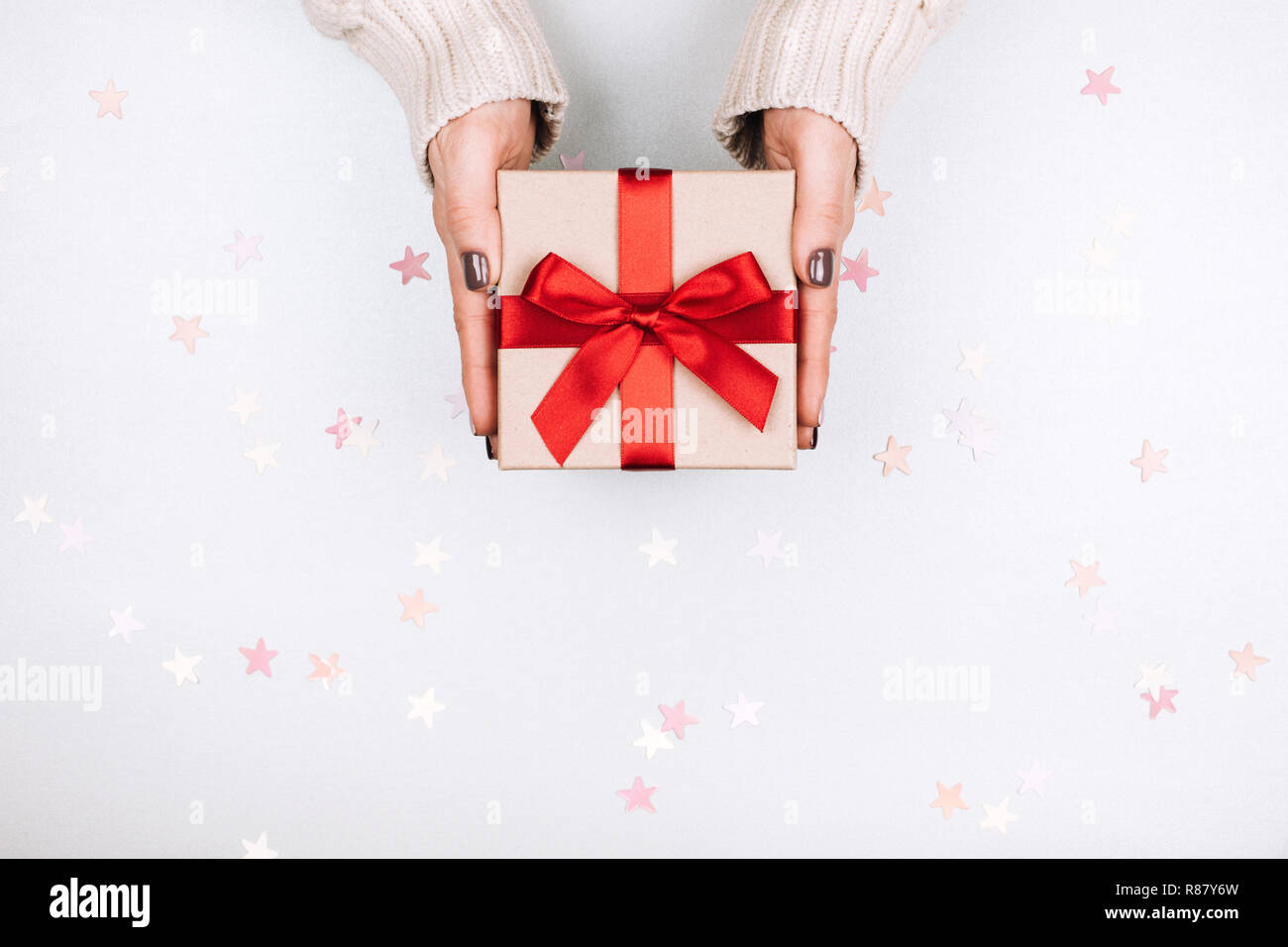 Woman hands holding present box with red bow on pastel blue background ...
