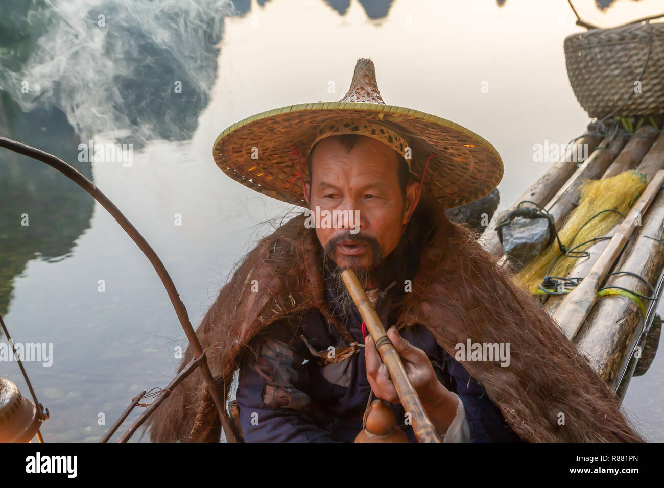 Chinese cormorant fisherman on raft in lake with pipe and fishing gear ...