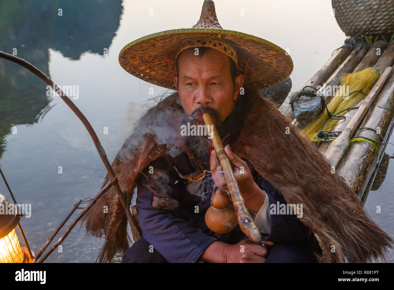 Chinese cormorant fisherman on raft in lake with pipe and fishing gear ...