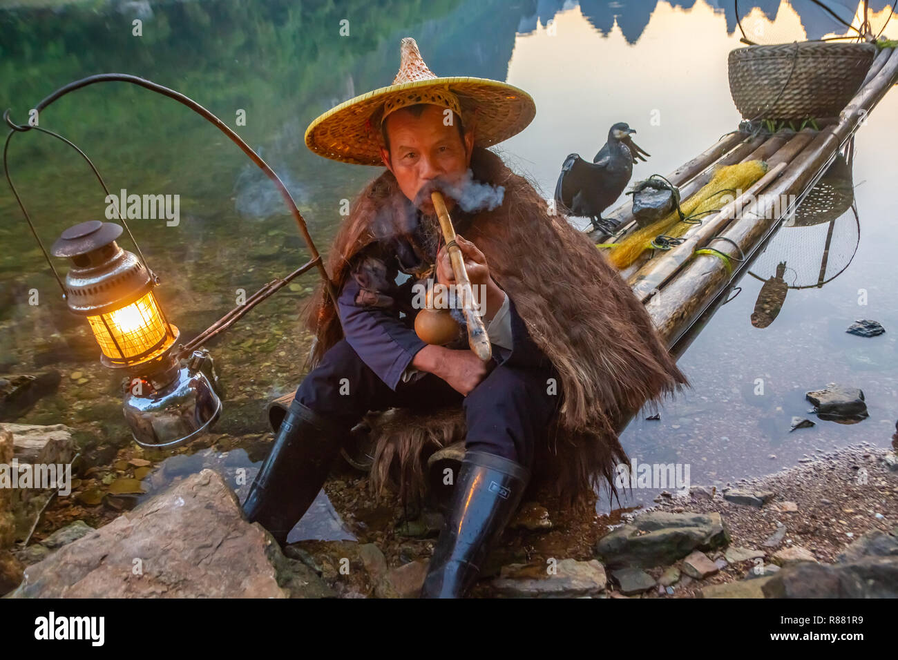 Chinese cormorant fisherman on raft in lake with pipe and fishing gear ...