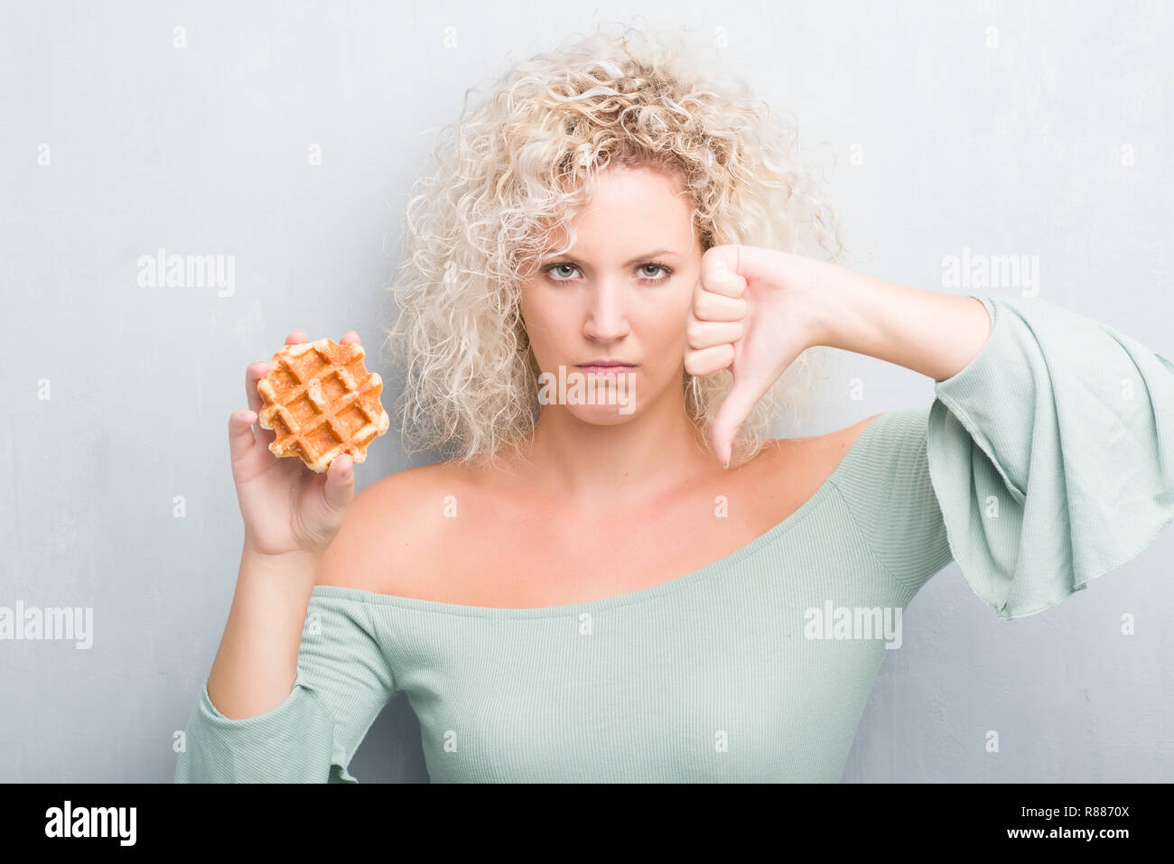 Young blonde woman over grunge grey background eating belgian waffle ...