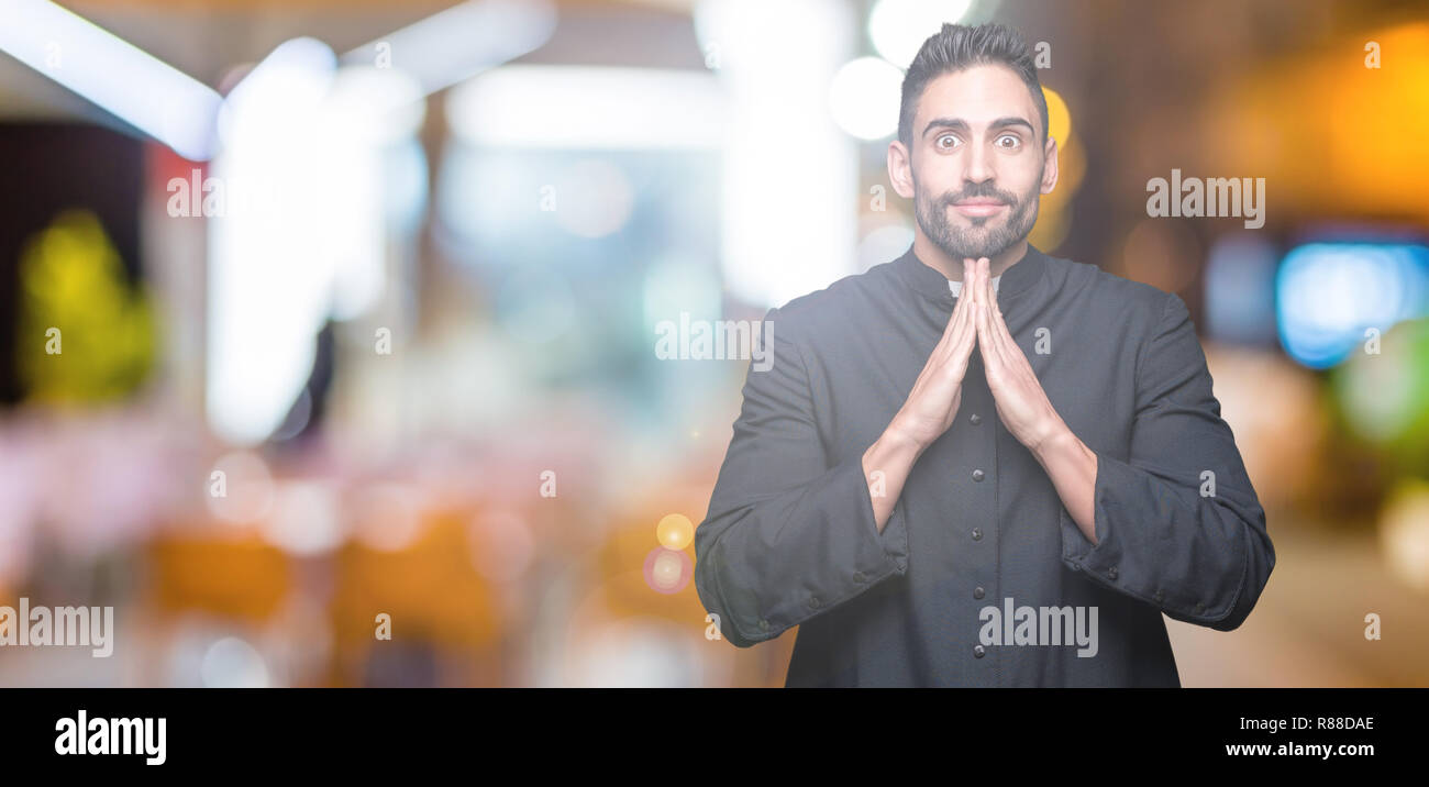 Young Christian priest over isolated background praying with hands ...