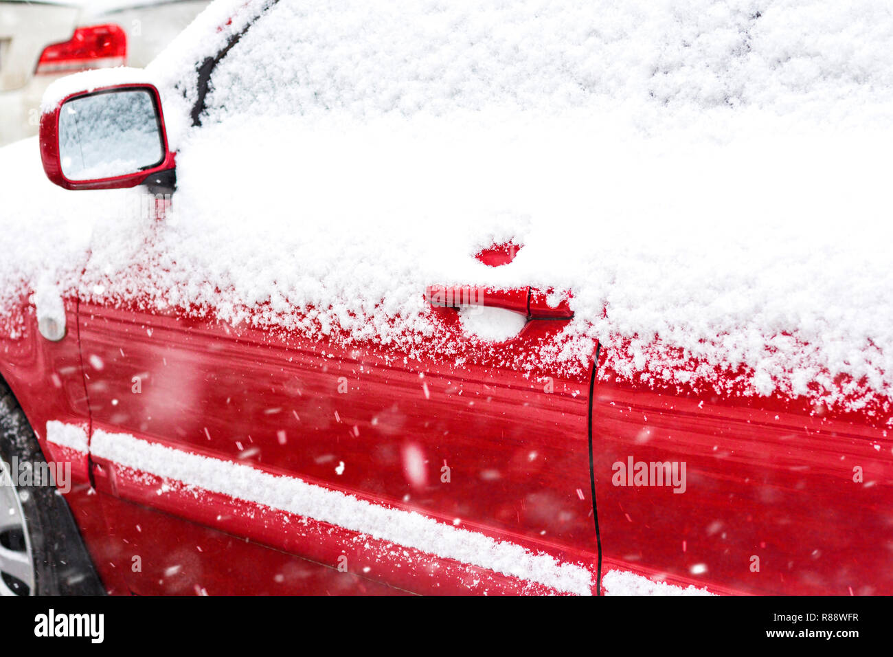 Snow-covered red car on parking in winter. View of a side mirror ...