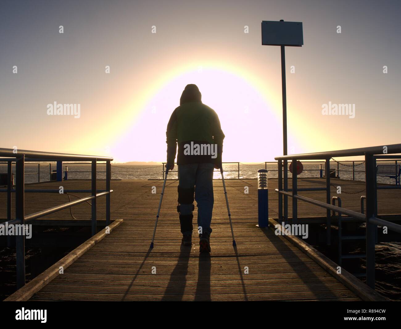 Hard walk of hurt man with crutches on port pier. Marwelous sunbreak at ...