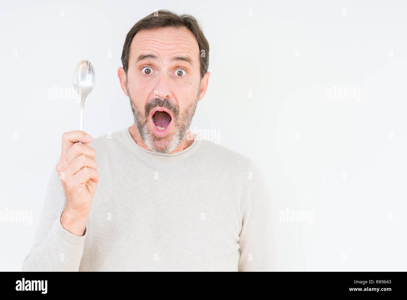 Senior man holding silver spoon over isolated background scared in ...
