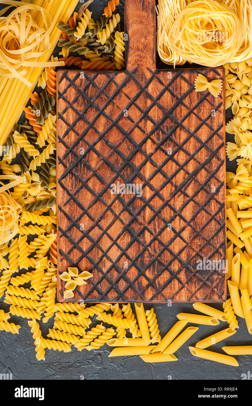 Assortment of raw types and shapes of italian pasta and wooden board on ...