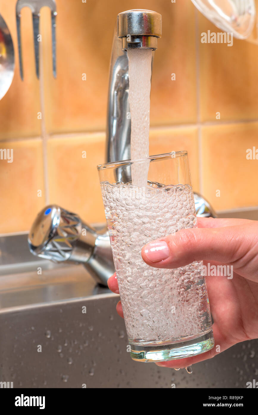 clean drinking water is poured from the kitchen tap into the glass ...