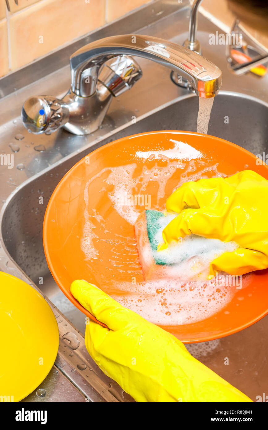 washing the orange plate with a sponge with foam in yellow gloves on ...