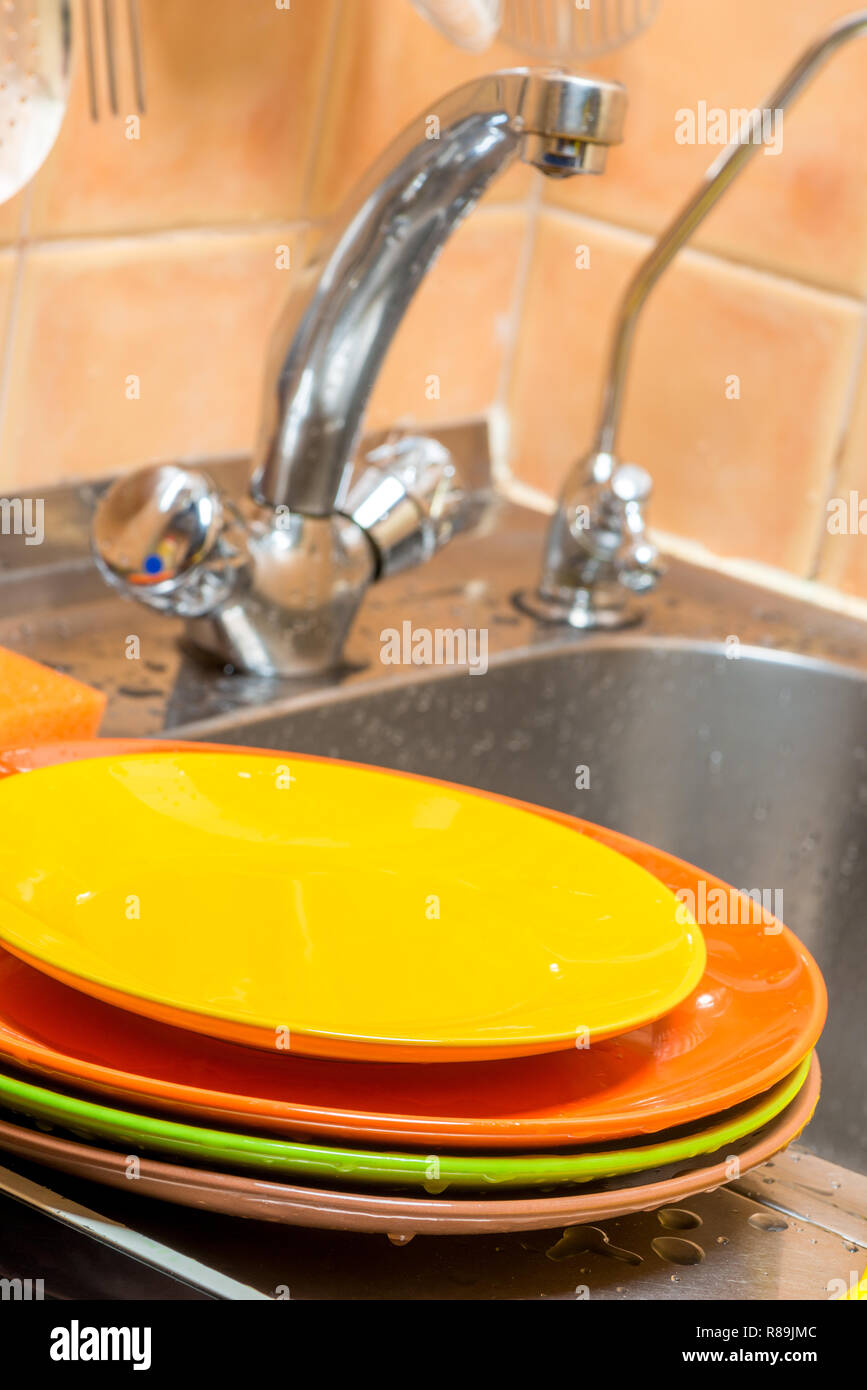 a stack of clean plates on the background of the sink and faucet in the ...