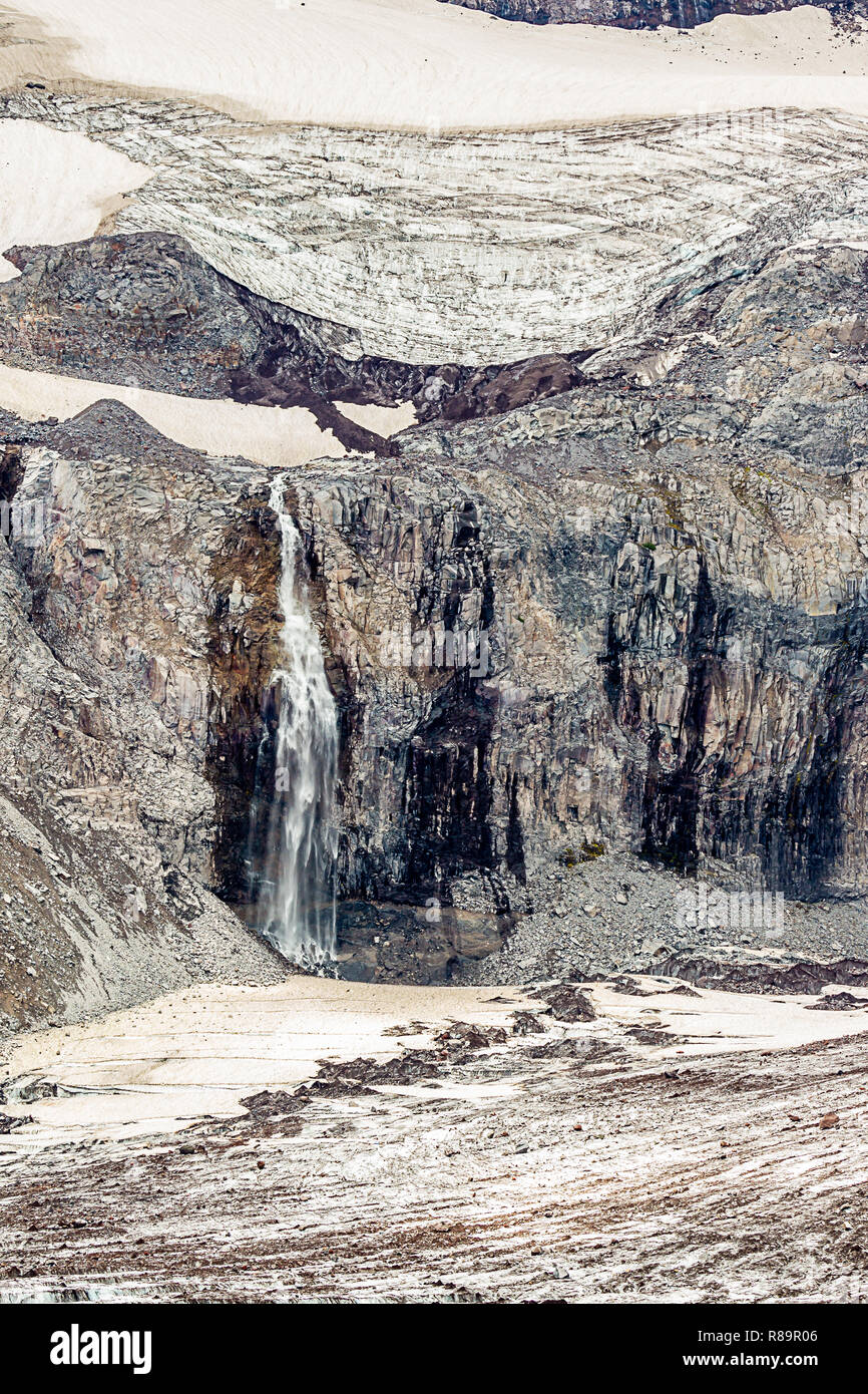 layers of snow ice and stone in front of a glacial waterfall in summer ...