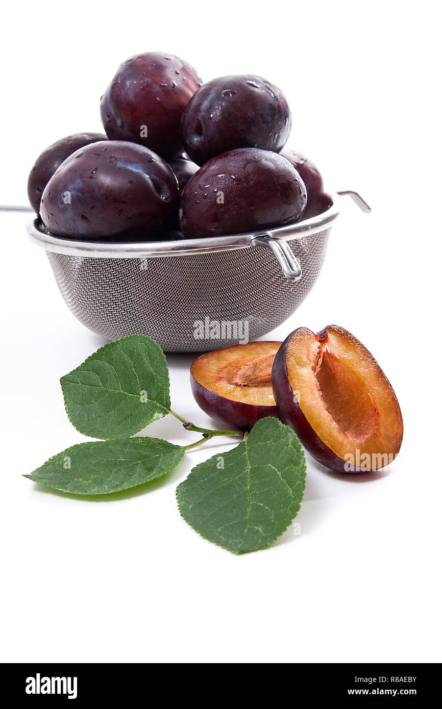 Steel colander with sweet juicy plums, whole and half ripe plums with ...
