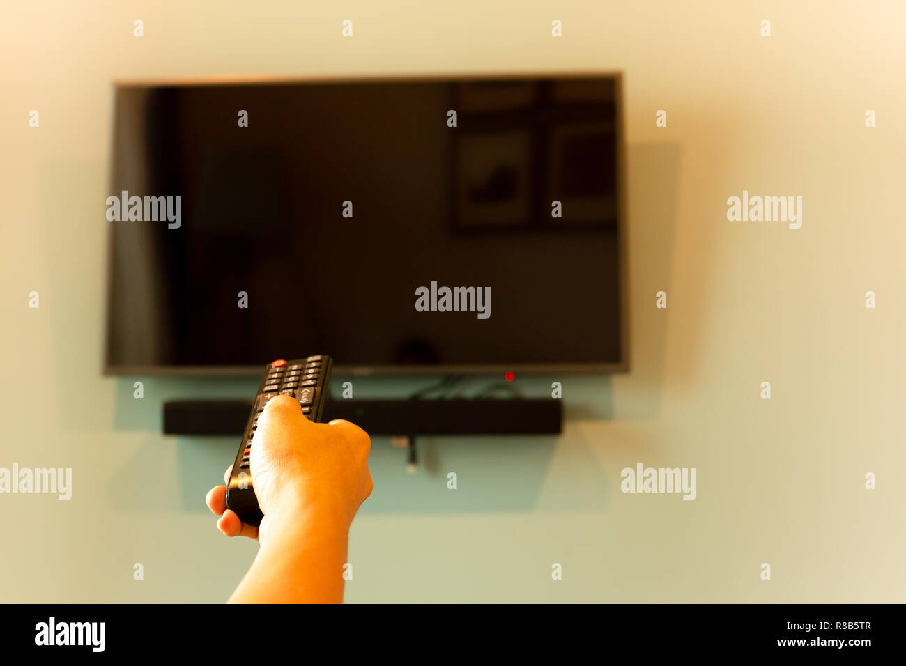 Hand holding TV remote control in front of widescreen TV set with blank ...