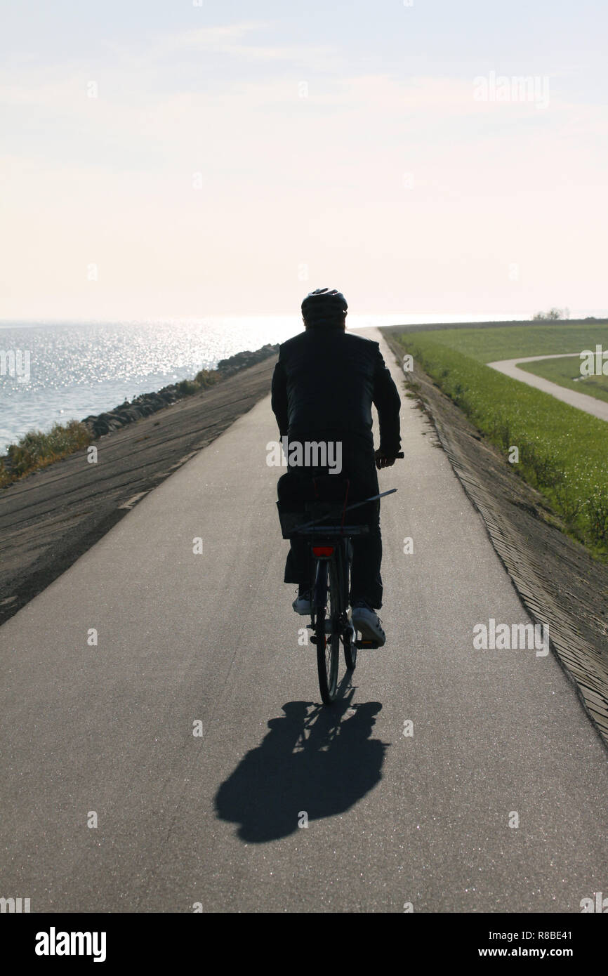 Male cyclist cyccling on a dam pier with ocean on one side and green ...