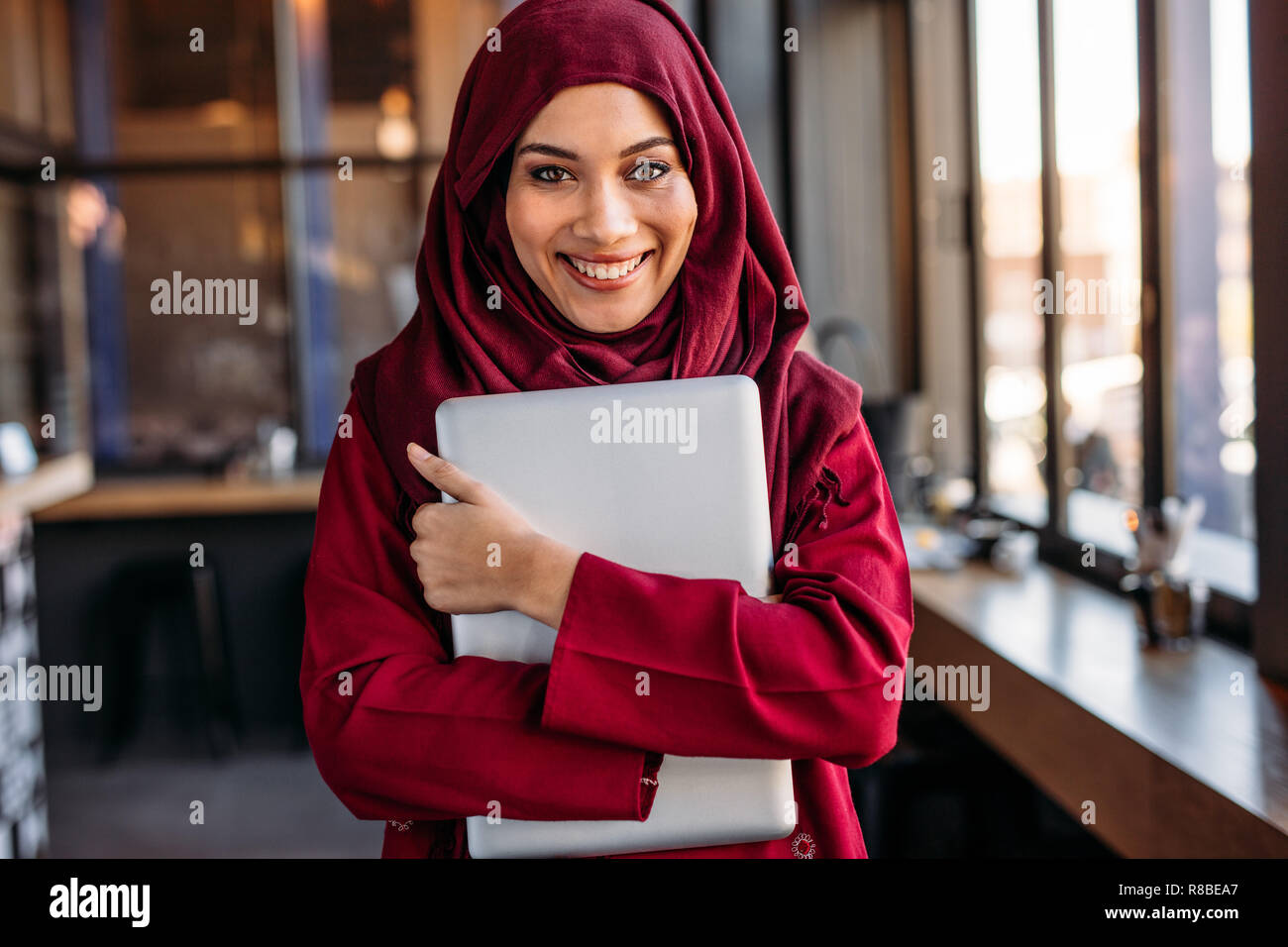 Cheerful islamic woman in hijab with laptop computer looking at camera ...