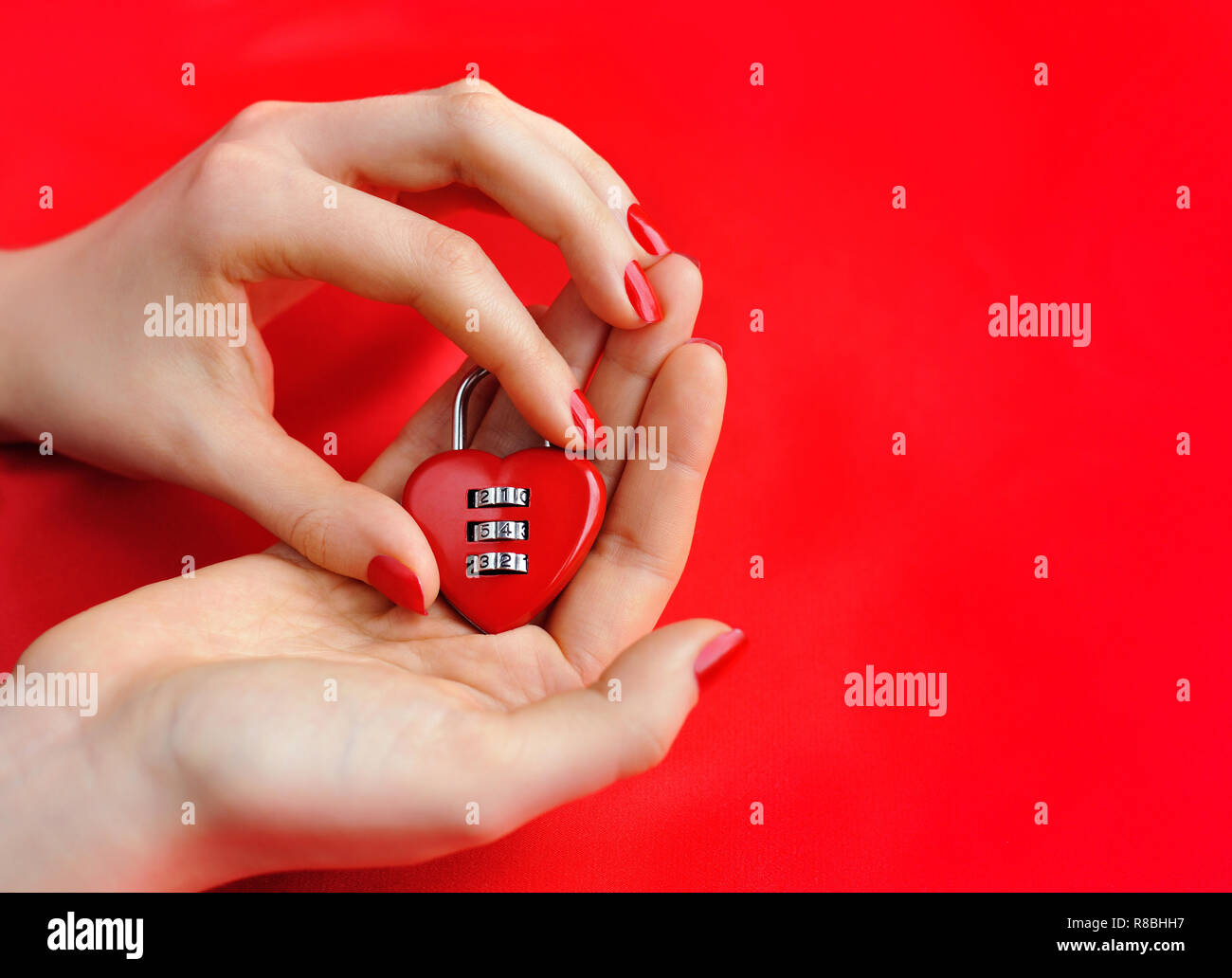 Padlock heart-shape in women's hands against a background of red silk ...