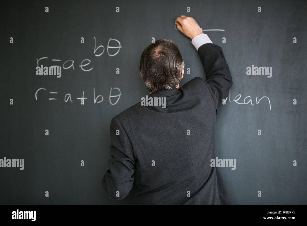 Senior male teacher teaching mathematics, writing on the blackboard ...