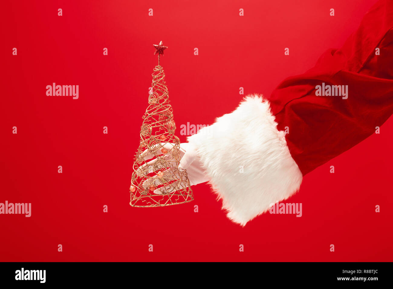 The hand of santa claus holding a toy christmas tree on red background ...
