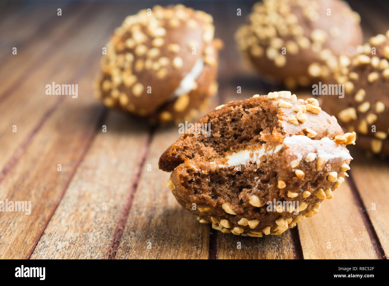 Biting off chocolate cookies with nuts and cream over wooden background ...